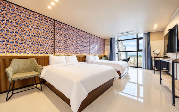 Quarto de hotel com duas camas, área de estar, escrivaninha e uma janela grande com vista.
