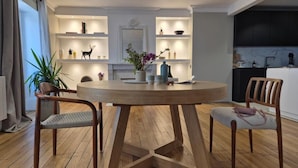 Uma área de refeições com uma mesa de madeira redonda, duas cadeiras e um vaso de plantas.