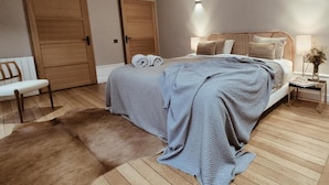Quarto com cama, duas portas, uma cadeira, mesa de cabeceira e abajur.