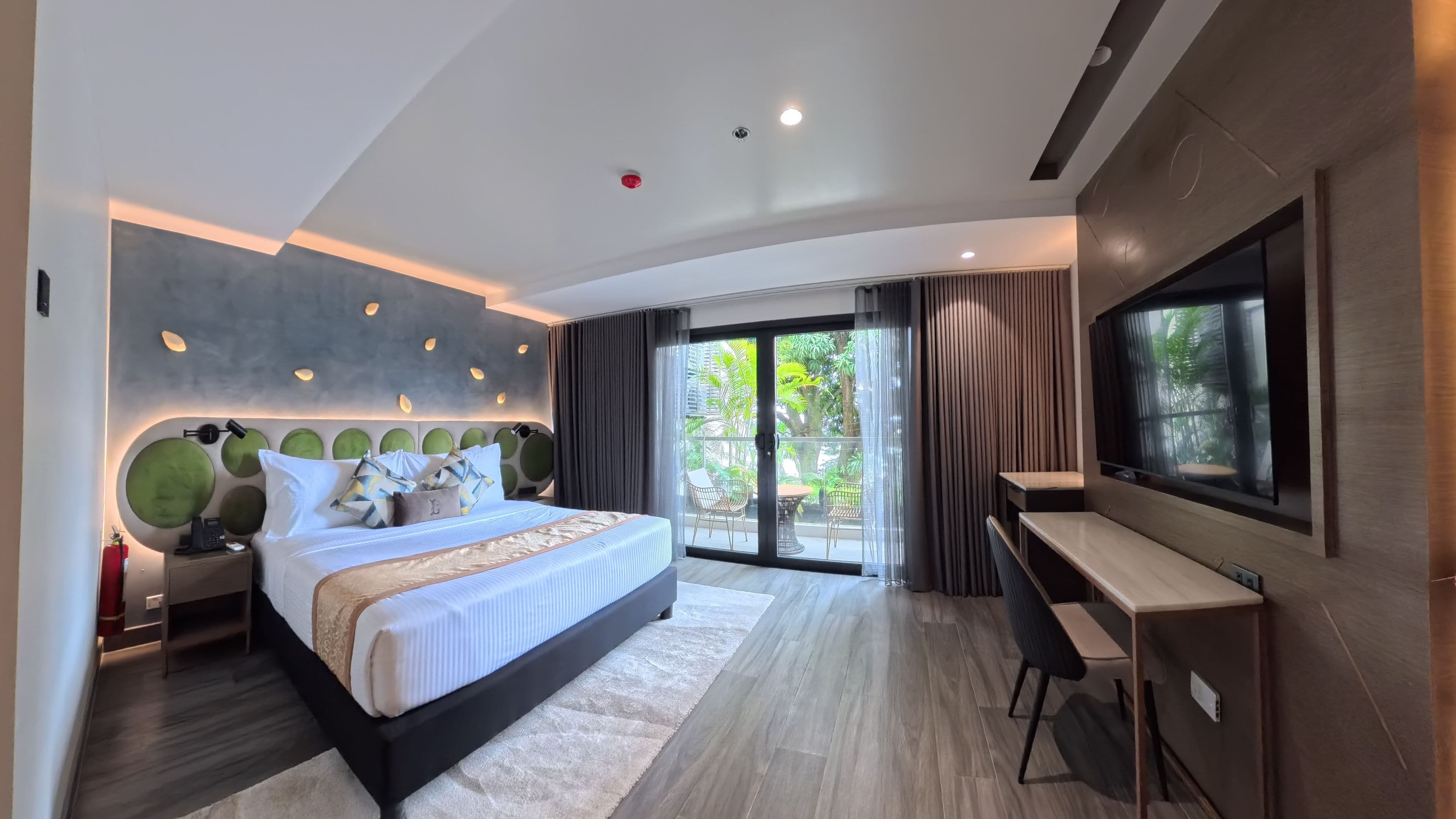 Quarto de hotel moderno com uma cama grande, uma escrivaninha, televisão de tela plana e porta de vidro que se abre para uma varanda.