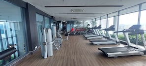 Ginásio com máquinas de cardio, equipamentos de peso e uma pessoa se exercitando.