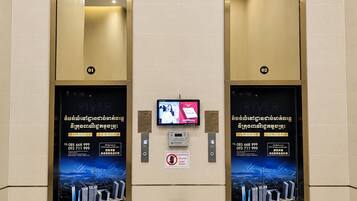 Interior de elevador moderno com painéis digitais, instruções de emergência e um anúncio de paisagem urbana.