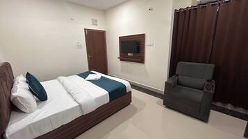 Quarto de hotel com cama, cadeira, televisão e porta.
