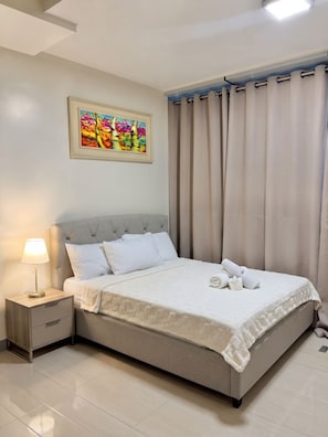 Cama bem arrumada com lençóis brancos, abajur e um quadro na parede.