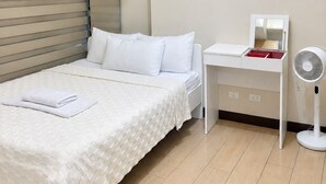 Quarto com cama, mesa de cabeceira e ventilador.