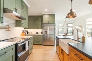 Cozinha moderna com armários verdes, eletrodomésticos de aço inoxidável e bancada de madeira.