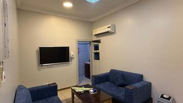Uma sala de estar com dois sofás, uma mesa de centro, uma TV de tela plana e um aparelho de ar condicionado.