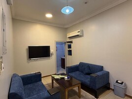 Uma sala de estar com dois sofás, uma mesa de centro, uma TV de tela plana e um aparelho de ar condicionado.