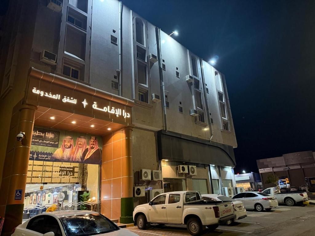 Um edifício com uma placa em árabe, vários andares e carros estacionados na frente.