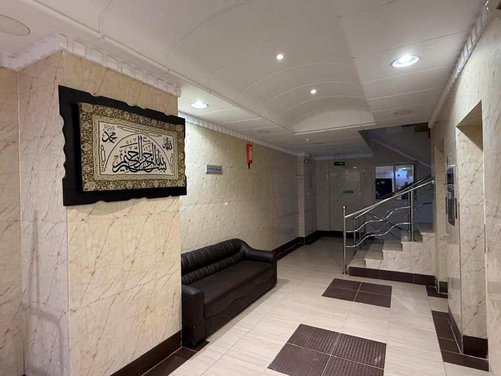 Um saguão com parede de mármore, sofá de couro preto e uma escada.