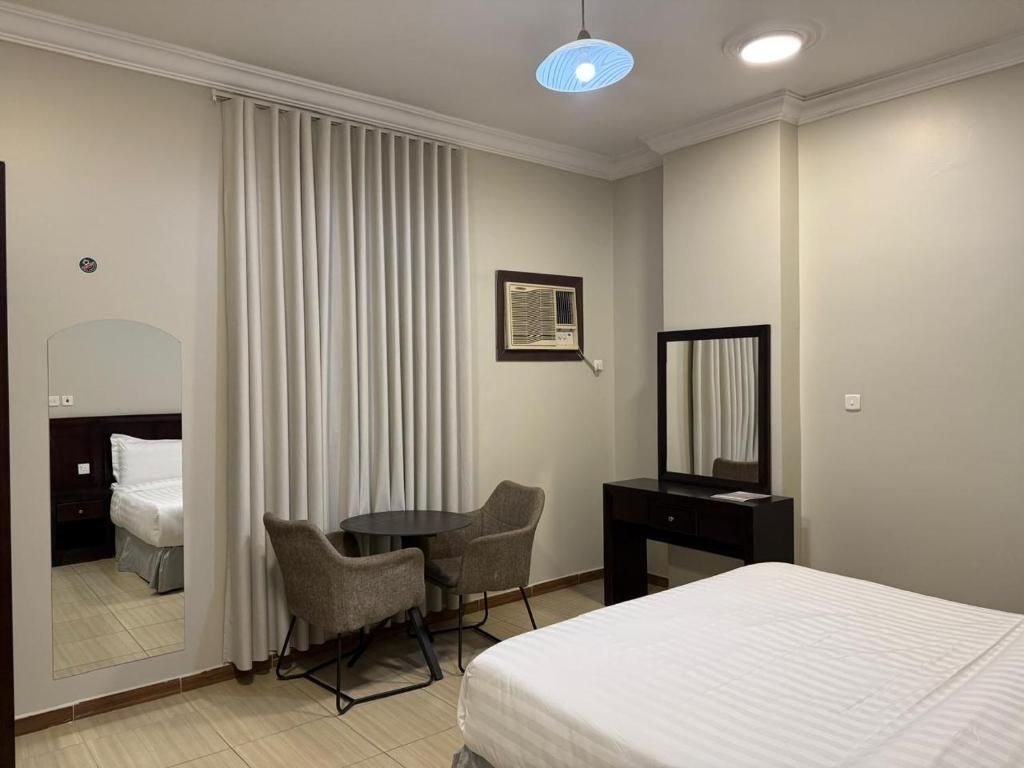 Quarto de hotel com cama, escrivaninha, cadeira, espelho e janela com cortinas.