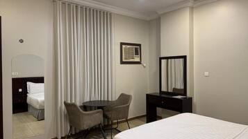 Quarto de hotel com cama, escrivaninha, cadeira, espelho e janela com cortinas.