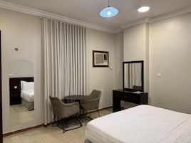 Quarto de hotel com cama, escrivaninha, cadeira, espelho e janela com cortinas.