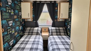 Interior compacto de um veículo recreativo, com duas camas, uma mesinha e uma janela com cortinas.
