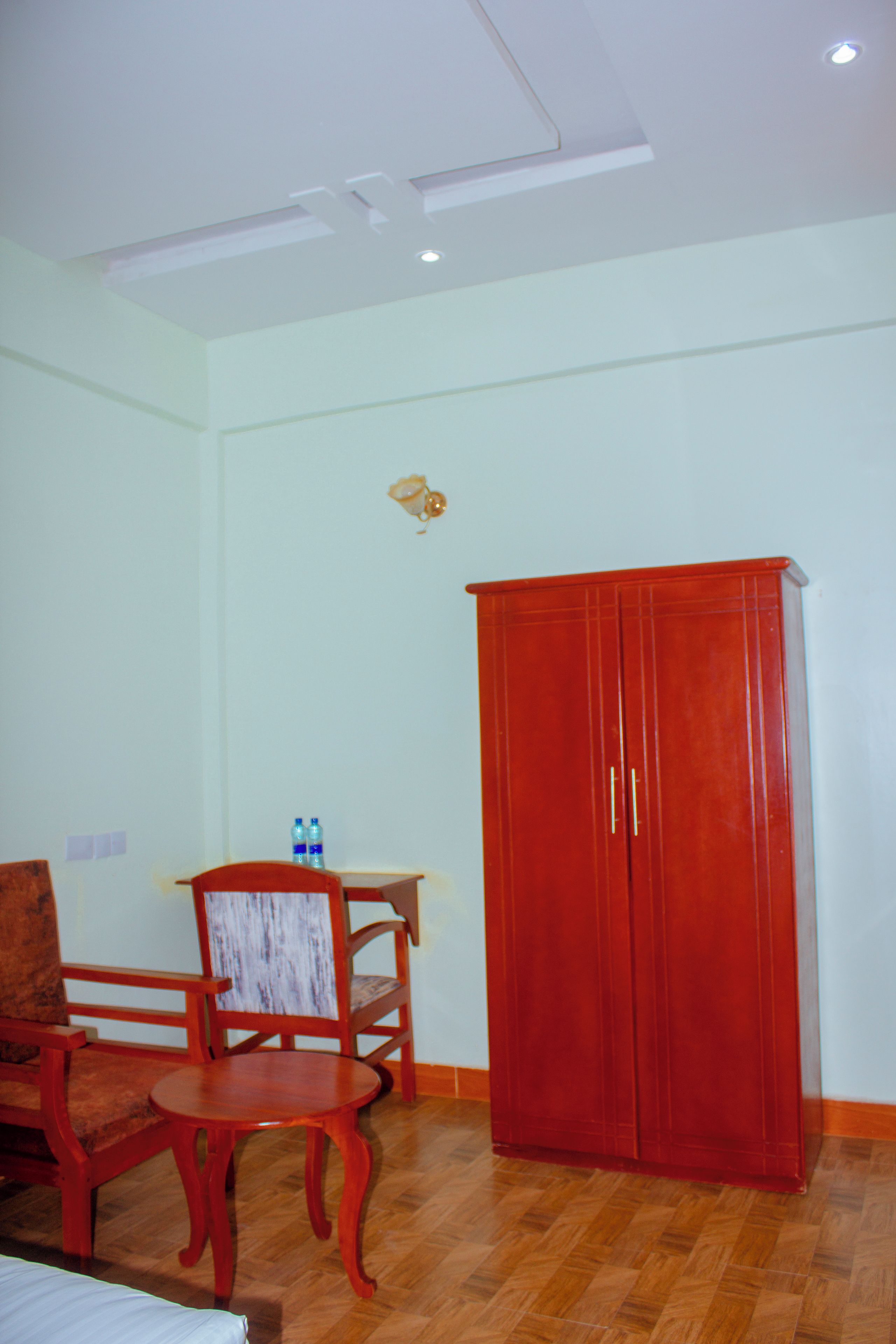Quarto com piso de madeira, guarda-roupa vermelho, cadeira de madeira e uma pequena mesa com duas garrafas.