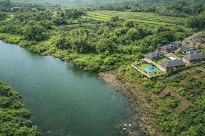 Vista aérea de uma propriedade à beira do rio, com piscina, várias casas e vegetação exuberante.