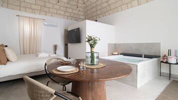 Quarto moderno com cama, mesa de jantar redonda, um vaso de vidro com flores, televisão de tela plana e uma banheira.
