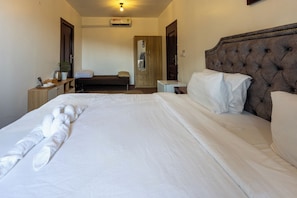 Quarto de hotel com uma cama grande, cabeceira de madeira, mesa de cabeceira, guarda-roupa e espelho.