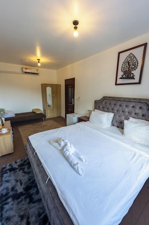 Quarto de hotel com uma cama grande, um guarda-roupa, uma mesa de cabeceira, um espelho e uma obra de arte emoldurada na parede.