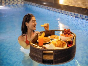 Uma pessoa em uma piscina segurando uma bandeja com comida e bebidas.