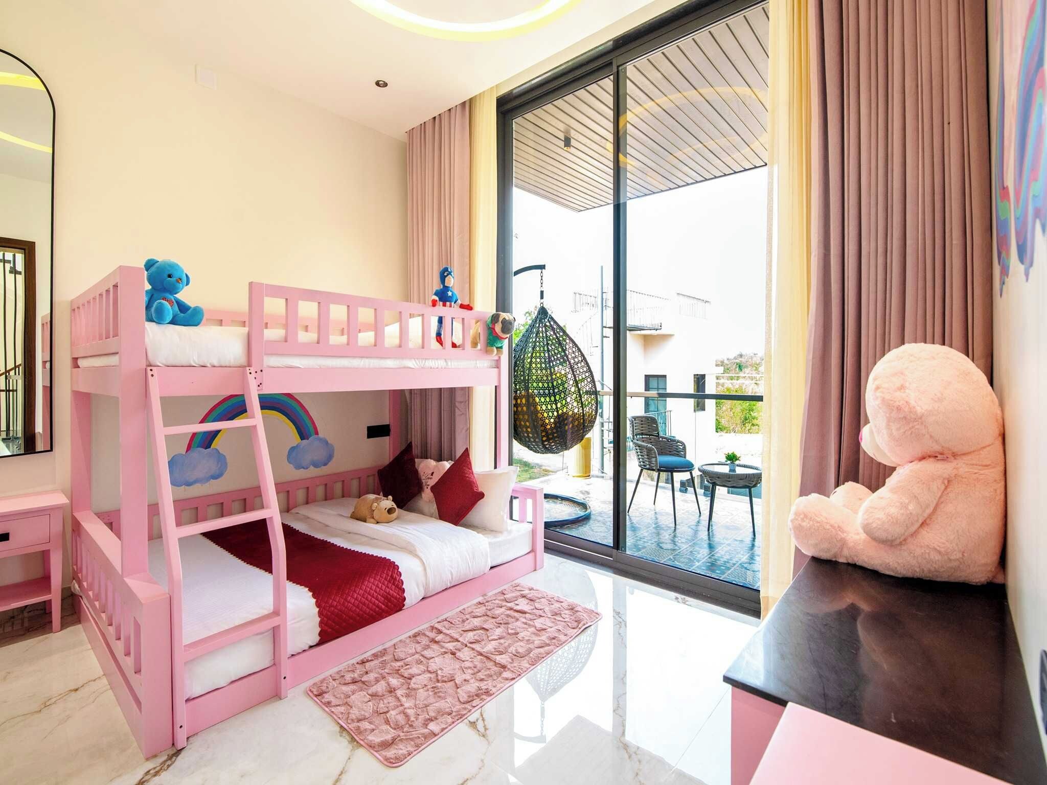 Uma cama beliche infantil com brinquedos, uma escrivaninha pequena e uma janela grande com vista para o exterior.