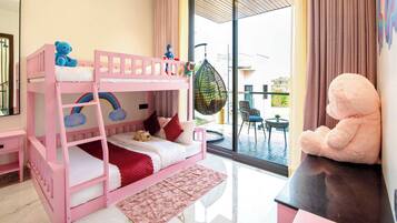 Uma cama beliche infantil com brinquedos, uma escrivaninha pequena e uma janela grande com vista para o exterior.