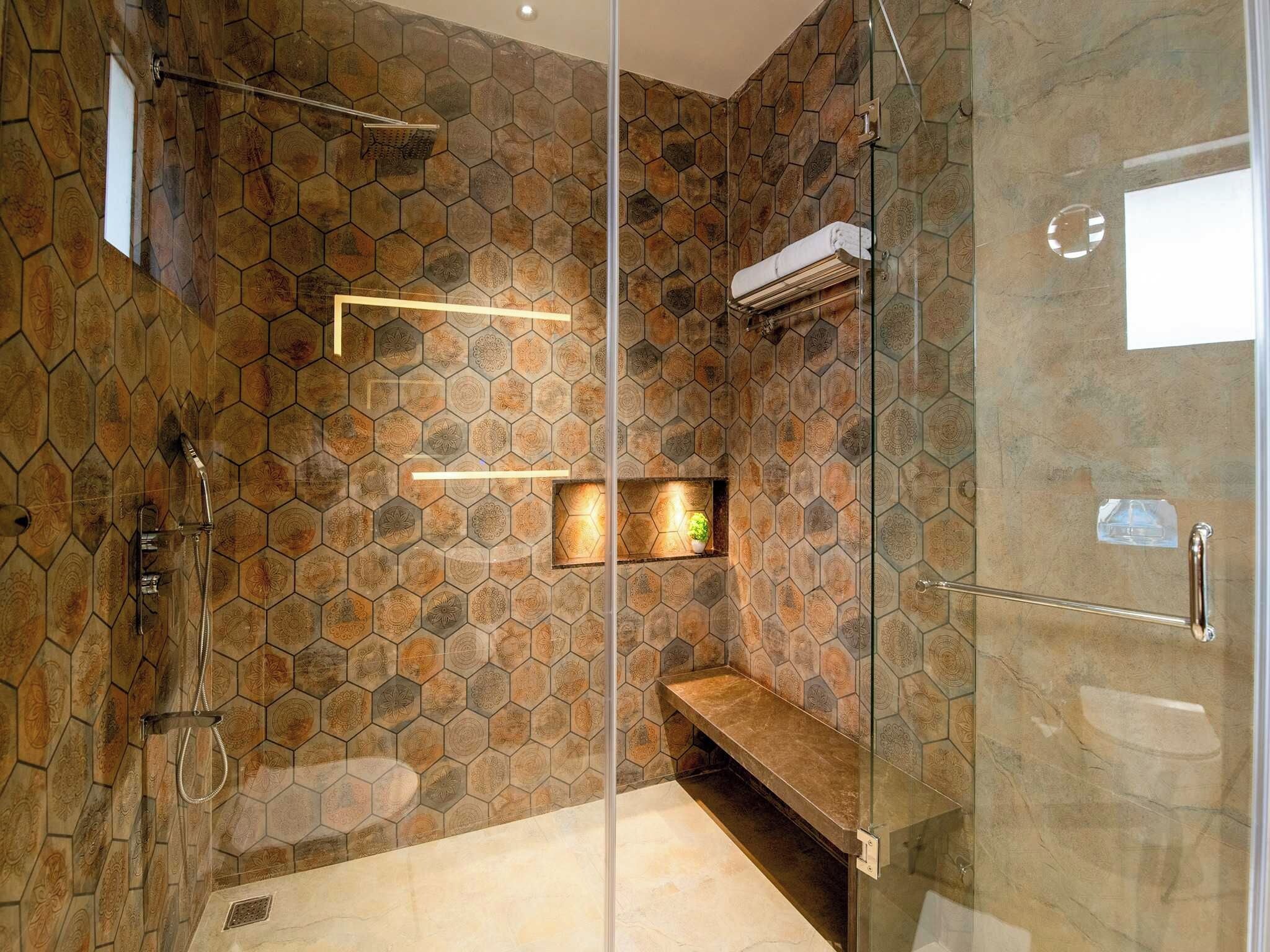 Área de chuveiro moderna com divisória de vidro, assento e parede com azulejos hexagonais.