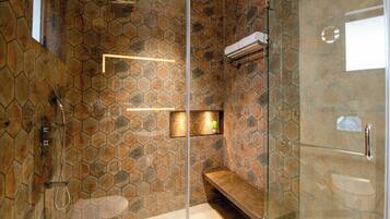 Área de chuveiro moderna com divisória de vidro, assento e parede com azulejos hexagonais.