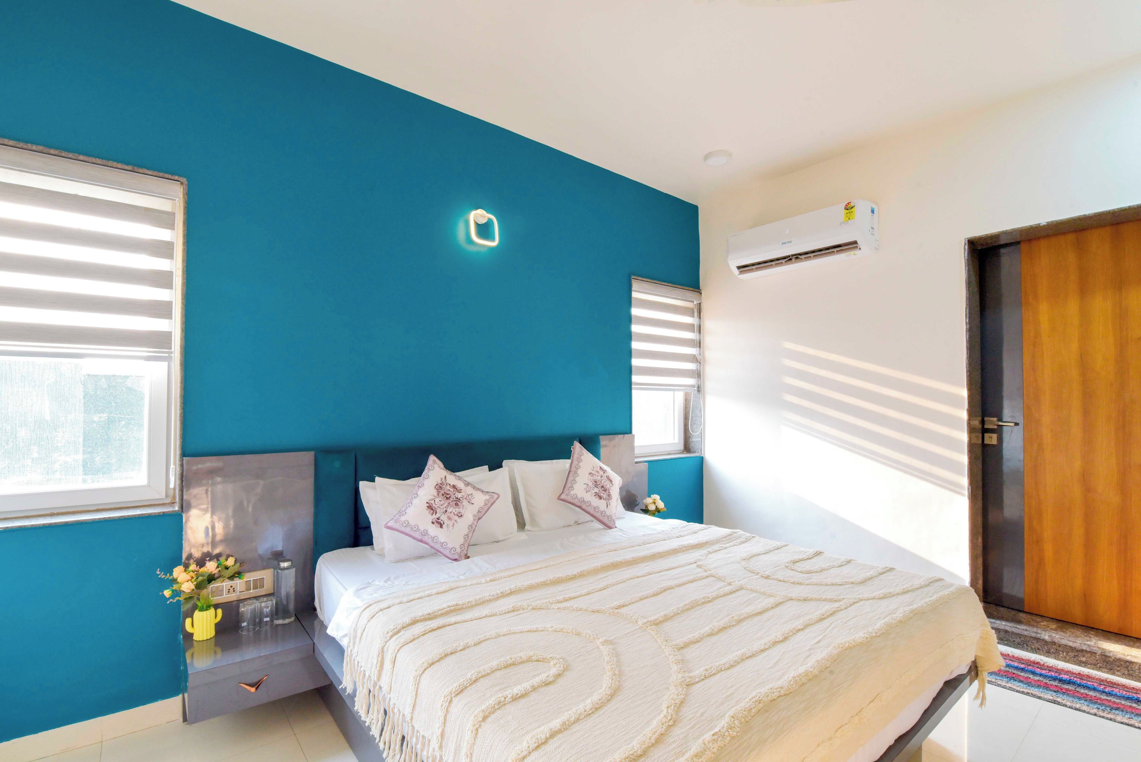 Quarto com cama, mesas de cabeceira, ar condicionado e janela com persianas, além de uma porta.