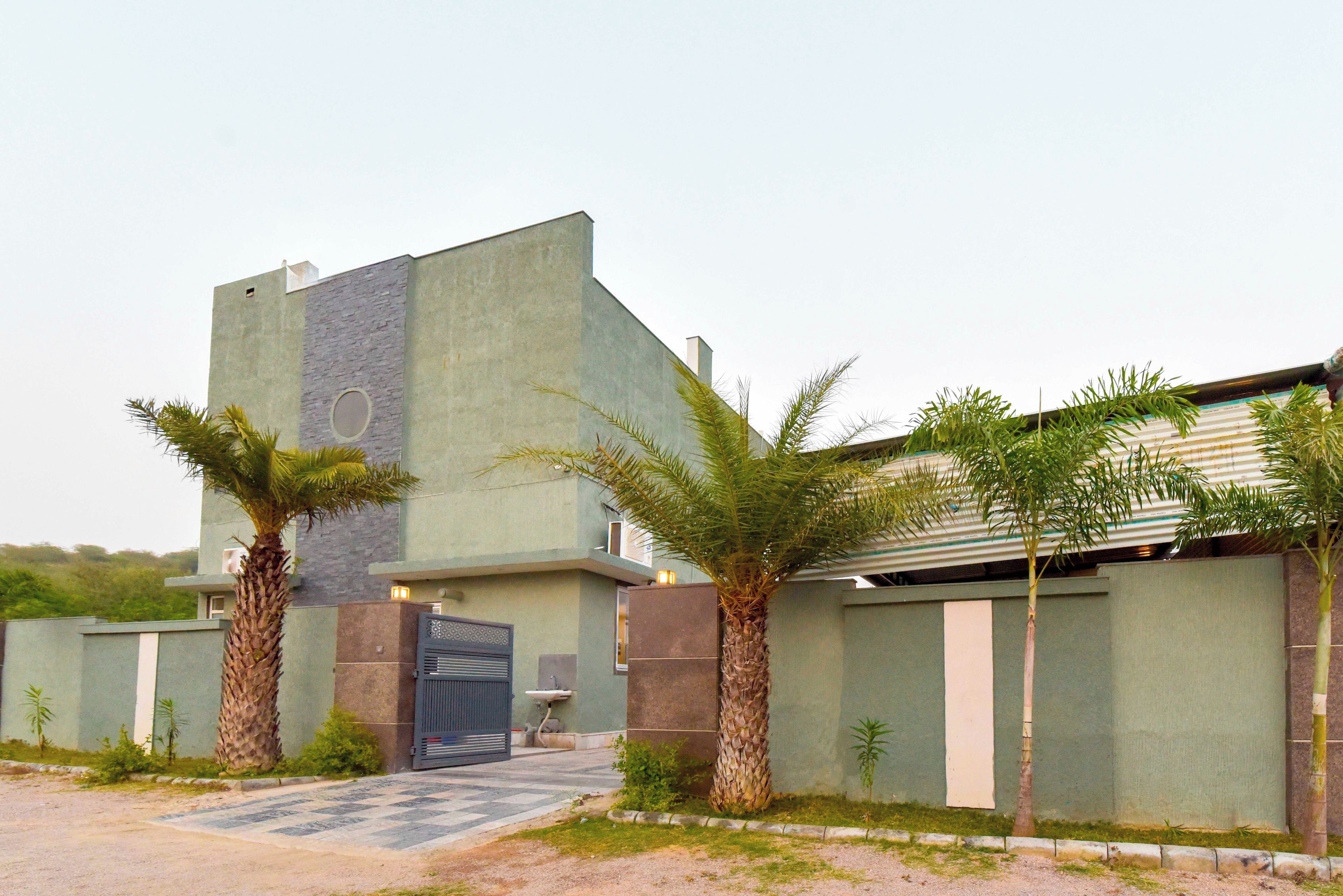 Um edifício moderno com fachada geométrica, entrada central e palmeiras em primeiro plano.