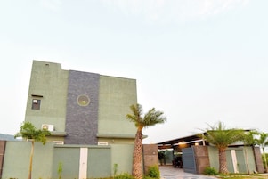 Um edifício moderno com telhado plano, elemento vertical central e área externa coberta com assentos.