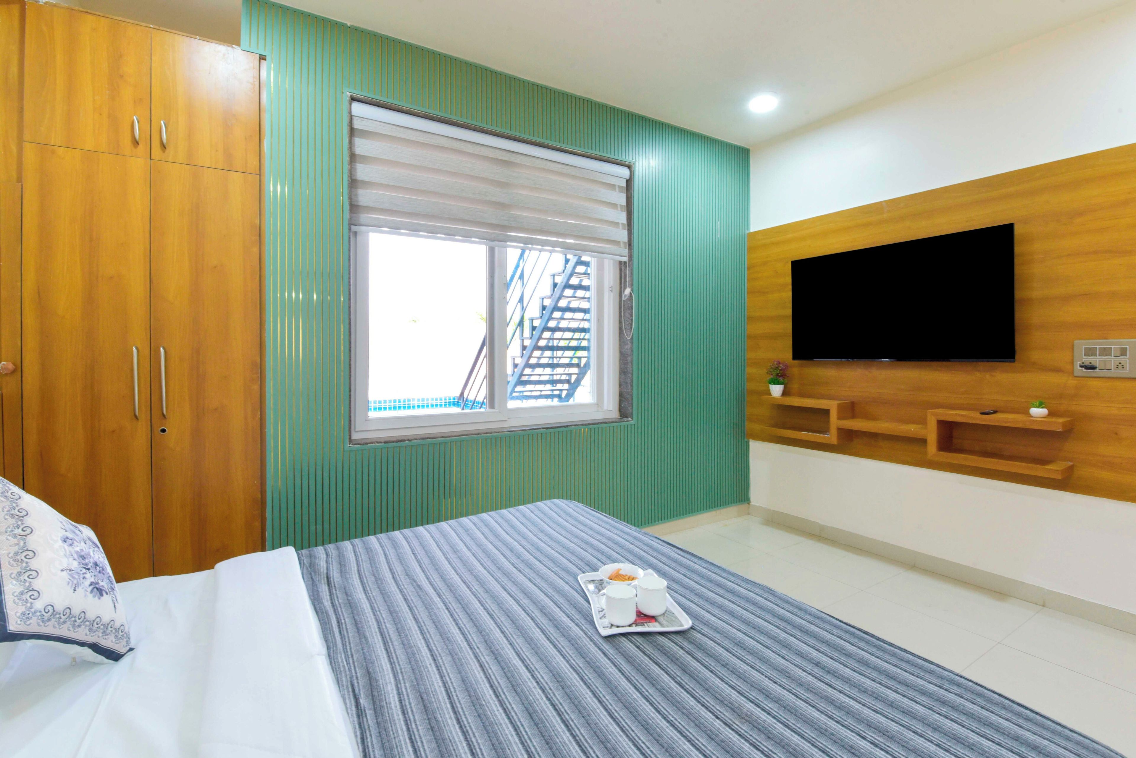 Quarto com cama, televisão, janela com persianas e guarda-roupa de madeira.