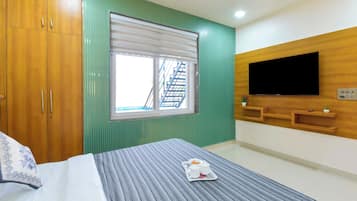 Quarto com cama, televisão, janela com persianas e guarda-roupa de madeira.