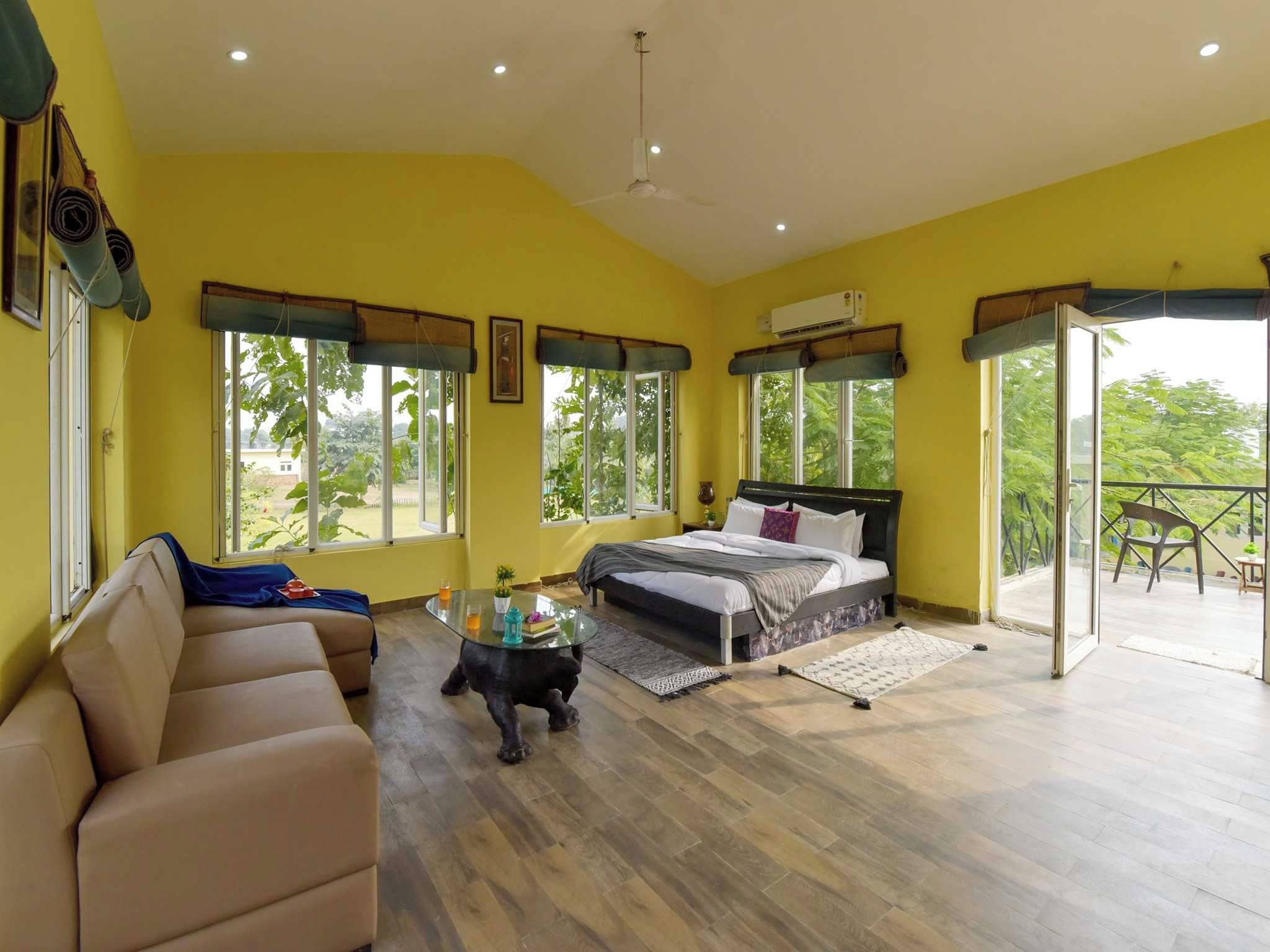 Quarto com cama, sofá, uma mesinha e grandes janelas.