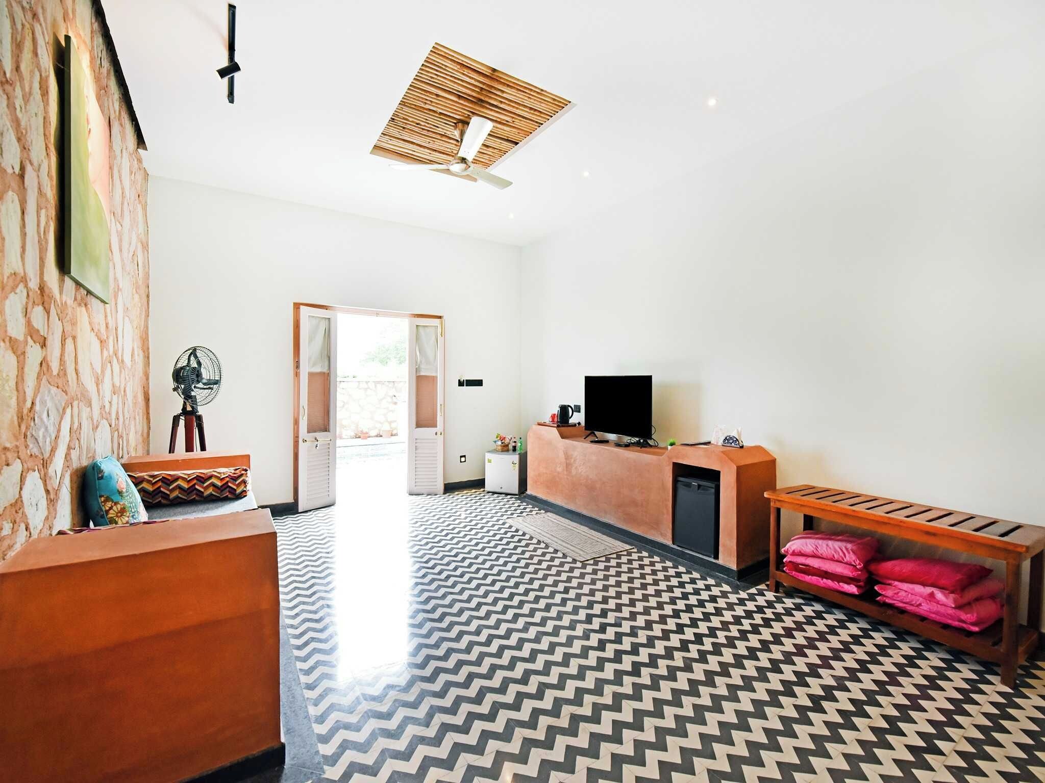 Quarto de hotel moderno com balcão de recepção, televisão, área de estar com piso estampado e porta para área externa.