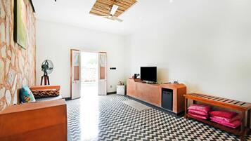 Quarto de hotel moderno com balcão de recepção, televisão, área de estar com piso estampado e porta para área externa.