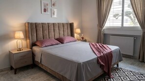 Quarto com cama, mesas de cabeceira, luminárias, janela com cortinas e radiador.