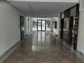 Um corredor com piso de mármore, porta de vidro e quadro de avisos fixado na parede.