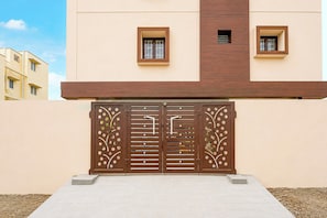 Um edifício moderno com fachada bege, duas janelas e um portão de metal decorativo com design geométrico.