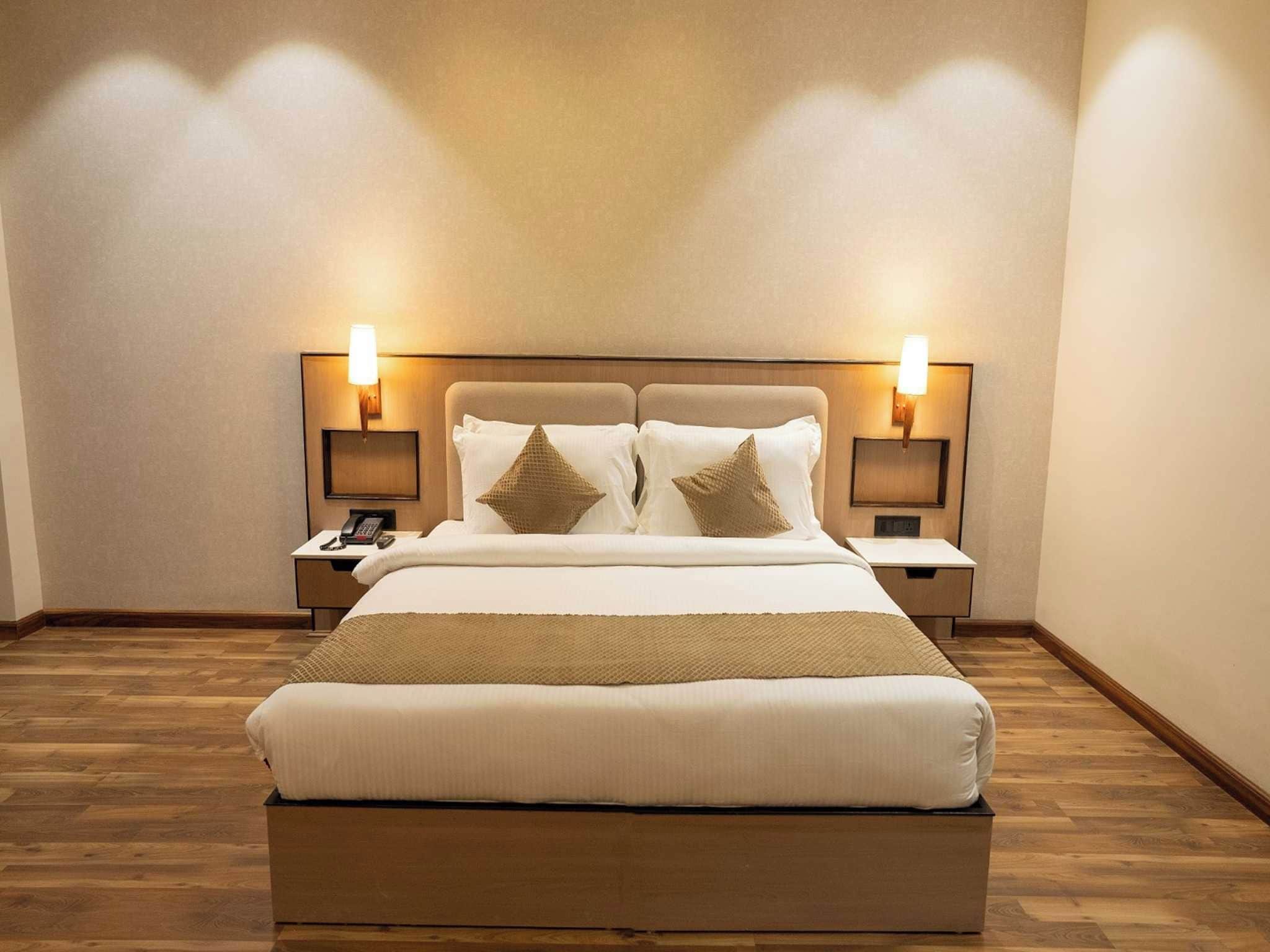 Quarto de hotel com uma cama grande, duas mesas de cabeceira e luminárias fixadas na parede.