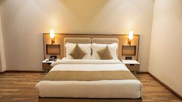 Quarto de hotel com uma cama grande, duas mesas de cabeceira e luminárias fixadas na parede.