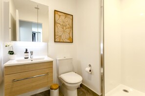 Um banheiro com pia branca, cômoda de madeira, vaso sanitário e chuveiro.