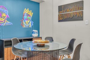 Uma sala de jantar moderna com uma mesa de vidro, cadeiras de vime e um quadro com uma vista da cidade na parede.