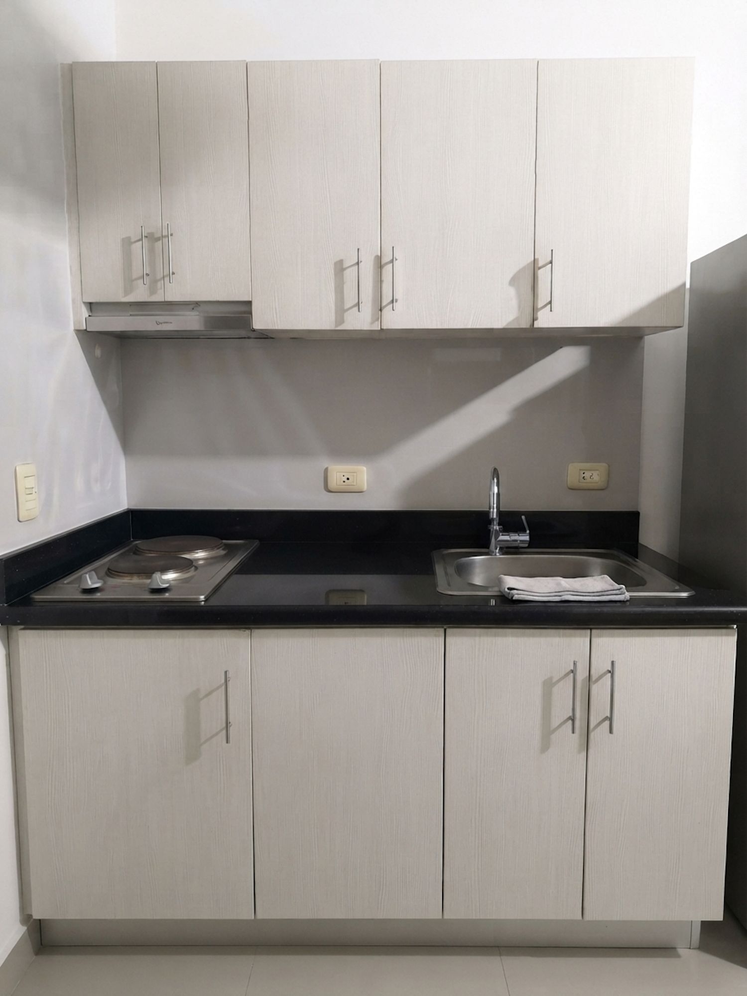 Cozinha com armários brancos, bancada preta e pia de aço inoxidável.
