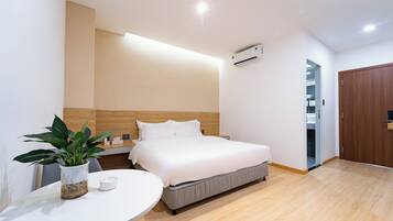 Quarto de hotel moderno com cama, mesa de cabeceira, planta em vaso e uma pequena mesa redonda.