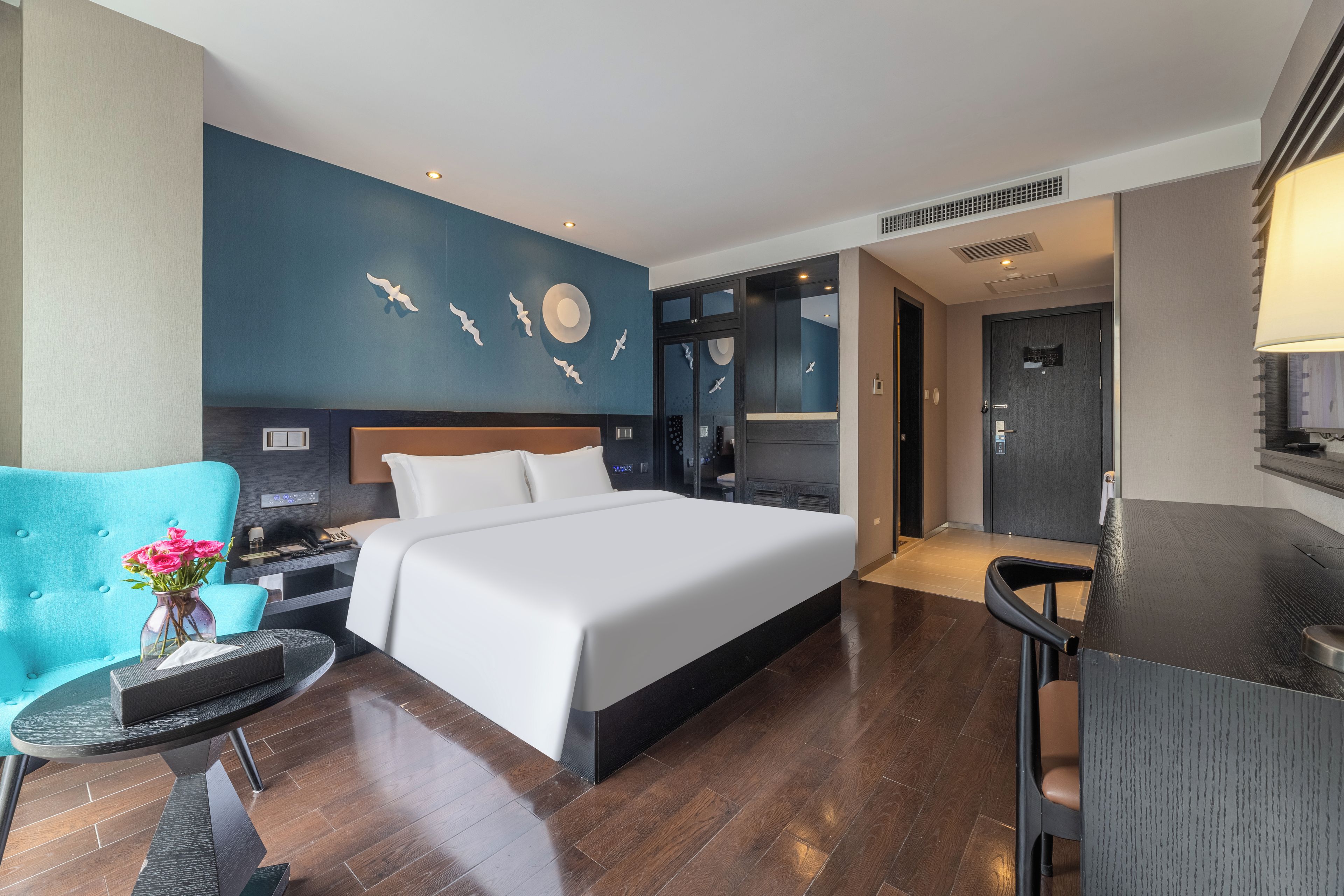 Quarto de hotel moderno com uma cama grande, área de estar com uma mesa, televisão e escrivaninha.