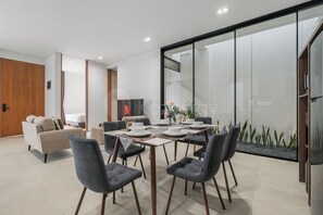 Uma área de refeições moderna com divisória de vidro, um conjunto de sofás e uma televisão de tela plana.