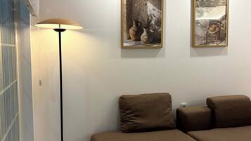 Quarto com sofá, luminária de chão e duas molduras na parede.