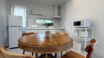 Uma cozinha moderna com uma mesa de madeira redonda, armários brancos, micro-ondas embutido e uma geladeira Samsung.