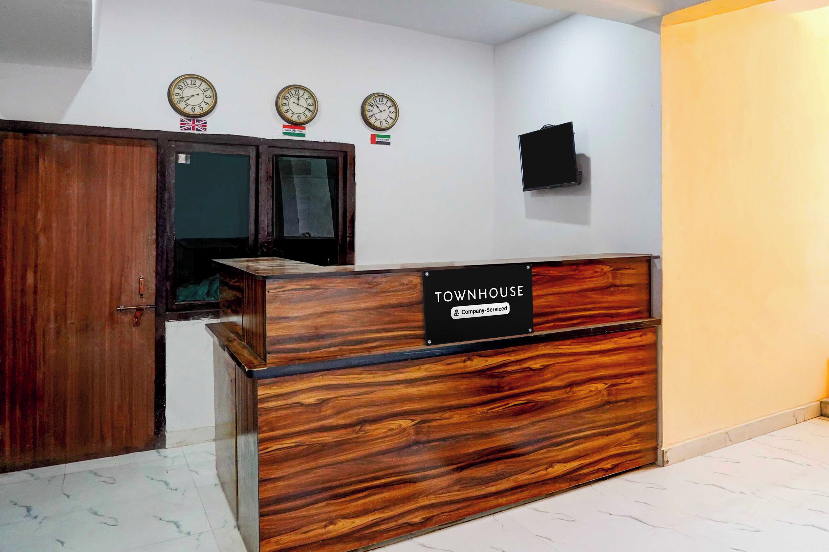 Bancada de recepção com placa indicando serviço da empresa, um armário de madeira e três relógios na parede.